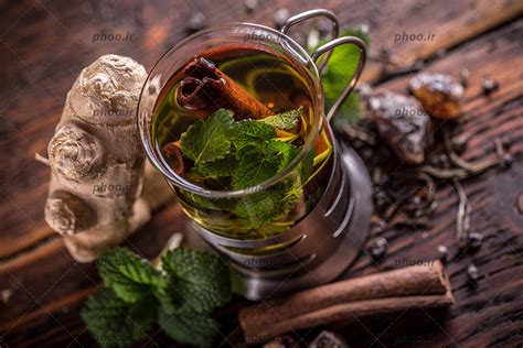 عکس با کیفیت یک فنجان دمنوش در کنار دارچین و نعناع و رنجبیل در پس زمینه