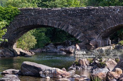 십 대 소녀는 Ulpha 호수 지역 국립 공원 영국에 있는 오래 된 돌 다리로 강 Duddon에 입력 됩니다 화창한 여름 날에 영국 시골의 아름 다운 보기 강에 대한 스톡