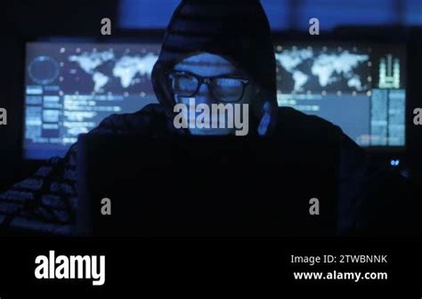 Man Geek Hacker In Hood With Glasses Working At Computer While Blue Code Characters Reflect On