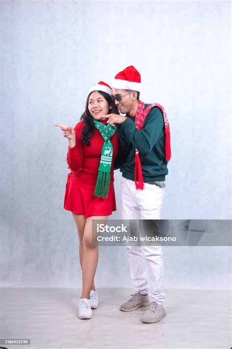 전신 산타 모자와 따뜻한 옷을 입은 두 명의 아시아 인 행복하게 왼쪽을 가리키며 서 있고 흰색 배경에 고립 된 크리스마스와 새해를 축하합니다 20 24세에 대한 스톡 사진