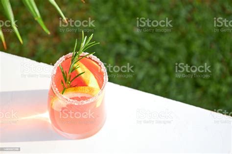밝고 화창한 날에 야자수 가지 아래 테이블에 얼음과 로즈마리 장식을 곁들인 차가운 자몽 칵테일의 최고 전망 여름 감귤류 음료