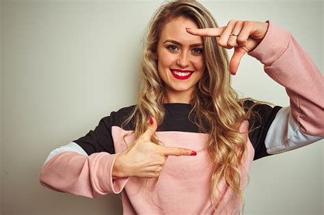 행복한 얼굴로 손과 손가락으로 프레임을 만드는 흰색 고립 된 배경 위에 서있는 스웨트 셔츠를 입은 젊은 매력적인 여성 창의력과 사진 개념 개념에 대한 스톡 사진 및 기타