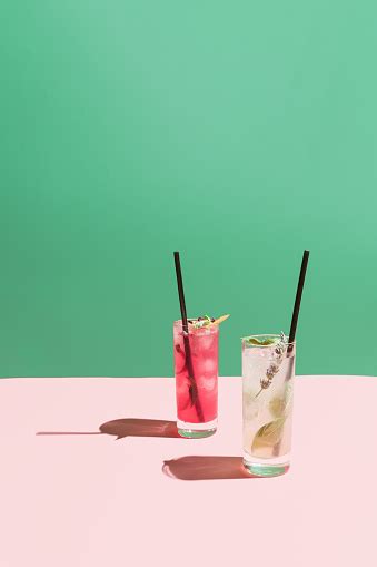 파스텔 핑크와 녹색 배경에 대한 빨대와 화창한 날 그림자가있는 하이볼 안경에 두 개의 칵테일로 만든 최소한의 구성 바 및 여름 파티 개념 마실 것에 대한 스톡 사진 및 기타