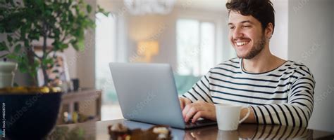 Foto De Handsome Adult Man Using Laptop Computer Sitting In Living Room And Drinking Tea Or