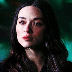 A Woman With Long Dark Hair Wearing A Black Shirt And Looking Off To