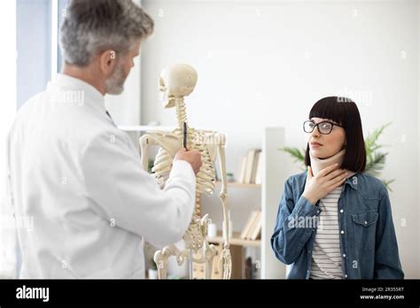 Over Shoulder View Of Beautiful Young Woman Wearing Neck Brace And Glancing At Human Skeleton