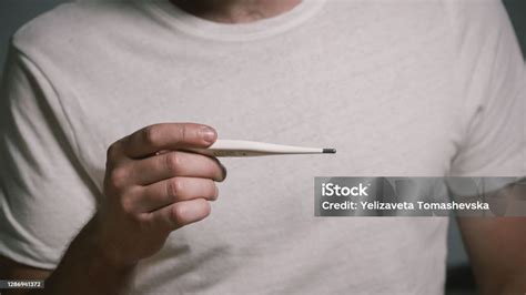 병에 걸린 아픈 남자가 발열을 느끼는 온도를 측정합니다 고온 개념 남자는 심하게 아프다 감기 증상과 원인 독감에 걸린 아픈 사람 남자는 온도계를 보유하고 있습니다 온도 측정