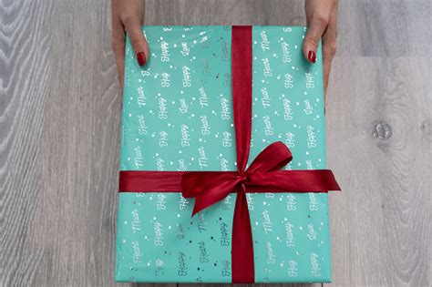 회색 나무 배경에 빨간 리본 활이있는 녹색 청록색 선물 상자를 들고있는 여자 손 개념 휴일 축하 생일 새해 크리스마스 발렌타인 데이 어머니의 날 추수 감사절 개념에 대한