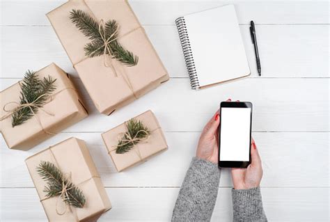 앱 프리젠 테이션 복사 공간을 위한 빈 화면이있는 휴대 전화와 여성의 손 흰색 나무 배경에 크리스마스 선물과 빈 노트북 플랫