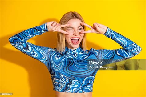 밝은 노란색 배경에 장난기 많은 손가락 제스처로 포즈를 취하며 행복과 자신감을 표현하는 세련된 파란색 상의를 입은 즐거운 젊은 여성 20 24세에 대한 스톡 사진 및 기타
