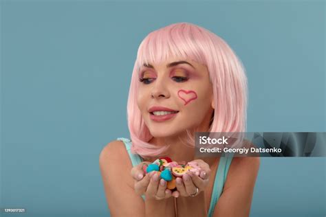 다양한 종류의 사탕을 들고 분홍색 가발을 쓰고 파란색 배경에 유혹적인 여성 모델을 클로즈업하십시오 예쁜 매력적인 여자 핑크 헤어 매력 과자 라이프 스타일 즐거움 설탕 가발에