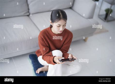 Asian Woman Controlling Smart Home Mobile Phone With Smart Home App In Living Room Touch