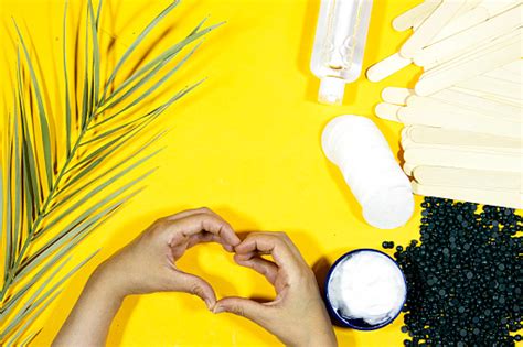 황량한 진주 색 고체 왁스 콩과 나무 막대기 면 패드와 크림 얼굴 상자 노란 배경에 심장 모양과 야자 수 잎을 만드는 손 여자 Waxing에 대한 스톡 사진 및 기타 이미지