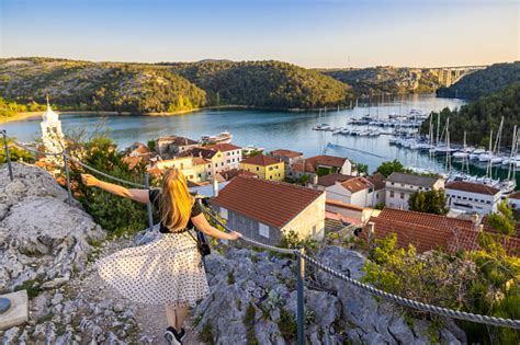 팔을 뻗은 여자가 언덕에 서서 항구가 있는 해안 마을을 바라보고 있다 35 39세에 대한 스톡 사진 및 기타 이미지 35 39세 40 44세 건물 외관 Istock