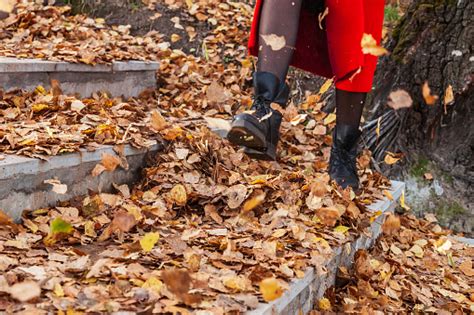 검은 색 부츠와 빨간 코트를 입은 소녀는 가을 동안 맑은 가을 날에 혼자 공원에서 산책하는 노란색과 붉은 단풍을 걷어차고 있습니다 신선함 자연 재미 10월에 대한 스톡 사진