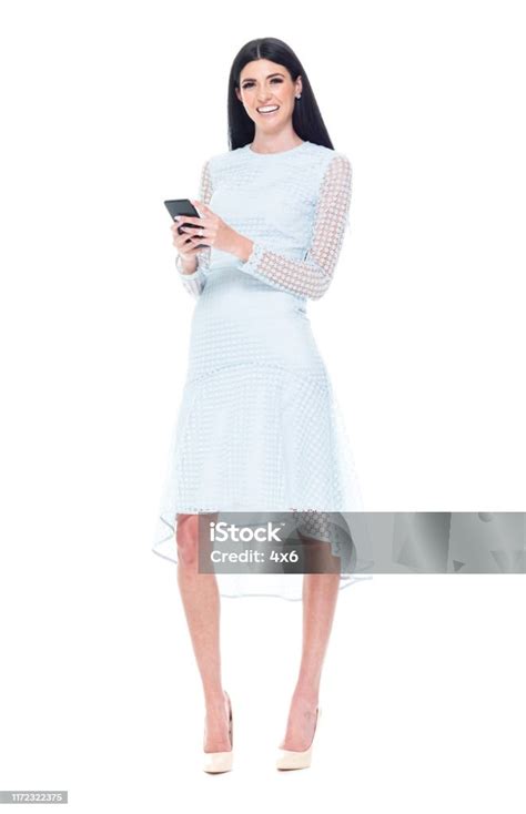전체 길이카메라정면보기 2029세 성인 아름다운 백인 젊은 여성여성 앞에 서서 웃고 있는 흰색 배경 옷입기행복쾌활한시원한 태도 휴대 전화를 들고 스마트폰에 대한 스톡 사진