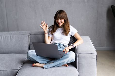 온라인 화상 통화 및 통신 가상 회의를 위해 노트북을 사용하여 웃는 여인의 초상화 집에서 소파에 앉아있는 웹캠에 손을 흔드는 친구 또는 가족과 이야기하는 모습 노트북에 대한