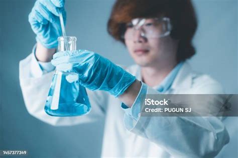 Scientist Hand Hold Erlenmeyer Flask With Stirring Rod Filled With Blue Sample Chemicals In