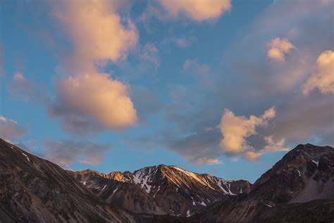 변화하는 날씨에 일몰 색상의 구름 아래 황금 햇빛에 날카로운 바위 절정높은 눈 산과 경치 하늘의 주황색 구름 아래 큰 산 꼭대기로 다채로운 경치 0명에 대한 스톡 사진 및