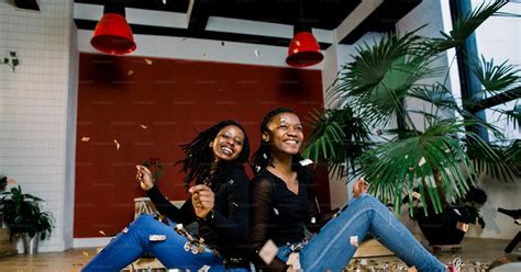 두 명의 아프리카 소녀 새해 또는 생일 파티를 축하하는 행복한 세련된 친구들이 서로 앉아서 색종이를 던집니다 함께 시간을 즐기는 패션 우아함 여성 사진