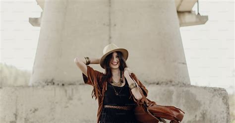 세련된 힙스터 여자는 강 돌 근처에 바람이 부는 머리를 가진 모자를 쓰고 재미있고 웃고 있습니다 집시 룩의 보헤미안 여행자