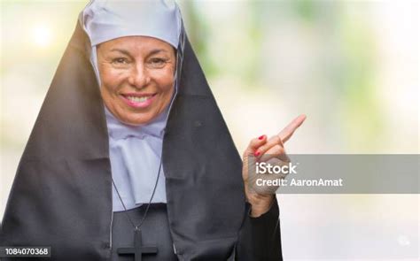 중 년 수석 기독교 가톨릭 수녀 여자 얼굴에 큰 미소와 함께 고립 된 배경 위에 카메라를 보고 옆에 손 및 손가락으로 가리키는 가리키기에 대한 스톡 사진 및 기타 이미지