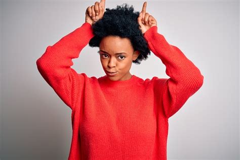 젊은 아름다운 아프리카 계 미국인 Afro 여자 곱슬 머리 를 입고 빨간 캐주얼 스웨터 를 하고 재미 제스처 와 손가락 위에 머리 로 황소 뿔 곱슬 머리에 대한 스톡 사진