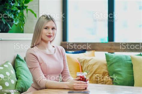 분홍색 드레스에 젊은 아름 다운 금발 소녀는 카페 테이블에 앉아 유리 항아리에서 음료 레모네이드 건강한 생활방식에 대한 스톡