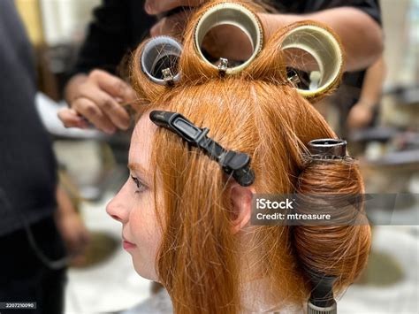 매력적인 빨간 머리의 여자 헤어 스타일링 알아볼 수없는 스타일리스트 드라이 젖은 머리 헤어 클립과 롤러 얼굴 샷 프로필 보기 전경에 초점을 맞춘 헤어 살롱 의자에 앉아 있는