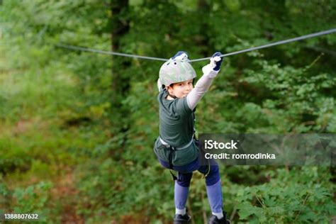 숲 모험 공원에서 학교 소년 헬멧을 쓰고 있는 아이는 높은 로프 트레일에서 올라간다 민첩성 기술과 어린이를위한 야외 놀이 센터를 등반 어린이 및 가족을위한 야외 활동 밧줄에
