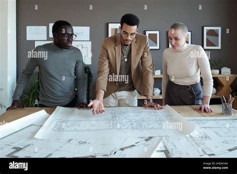 One Of Three Coworkers Making Presentation Of Large Sketch On Blueprint