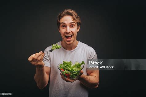 흰색 티셔츠를 입은 젊은 금발 남자가 검은 색 배경에 고립 된 샐러드의 행복한 접시를 들고 있습니다 25 29세에 대한 스톡 사진 및 기타 이미지 Istock