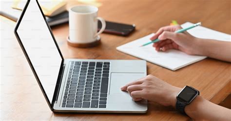 흰색 빈 화면 컴퓨터 노트북에 타이핑하고 커피 컵 스마트폰 노트북이 있는 현대적인 나무 테이블에서 노트북에 글을 쓰는 동안 비서 여성의 손이 잘린 이미지 사진