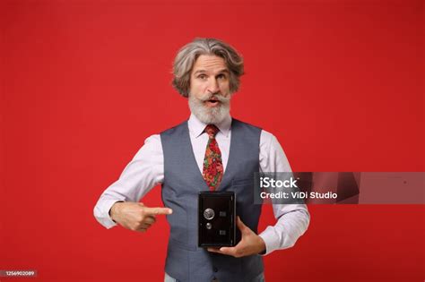 빨간 배경에 고립 된 클래식 셔츠 조끼 넥타이에 노인 회색 머리 콧수염 수염 남자 사람들 라이프 스타일 개념 복사 공간을 모의합니다 돈 축적에 대한 안전한 금속 은행에