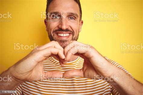 노란 고립 된 배경 위에 캐주얼 한 티셔츠를 입고 있는 젊은 잘생긴 남자의 가까이에서 하트 기호와 손으로 모양을 보여주는 사랑에 미소 로맨틱 한 개념 남자에 대한 스톡 사진