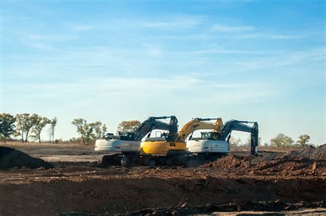 현대식 흰색과 노란색 굴삭기 3대가 푸른 하늘을 배경으로 도시 간 고속도로에서 도로 공사를 하는 동안 발굴된 땅에 서 있습니다 양동이가 있는 굴착기 3가지 개체에 대한 스톡