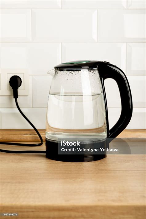 주방의 나무 테이블에 있는 현대적인 전기 투명 주전자 물을 끓이고 차를 만들기위한 주전자 뜨거운 음료를 만들기위한 가전 제품 복사 공간 텍스트를 위한 장소입니다 주전자에