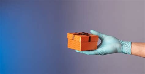 파란색 보호 장갑을 낀 남자의 손이 파란색과 회색 배경에 선물 상자를 들고 있습니다 전염병의 라이프 스타일 개념 35 39세에 대한 스톡 사진 및 기타 이미지 Istock