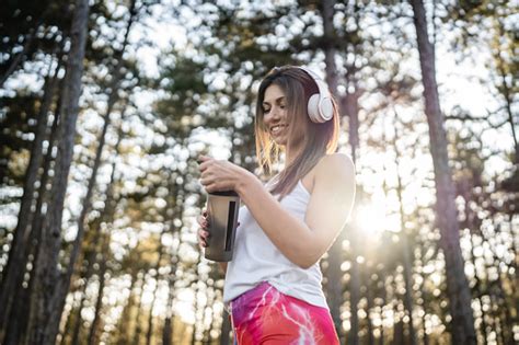 한 여성 행복한 백인 여성 숲이나 숲에 공원에 서서 자연 훈련을하는 동안 보충 쉐이커와 헤드폰으로 브레이크 워터 음료와 수분 공급 실제 사람들은 공간을 복사합니다 개념에