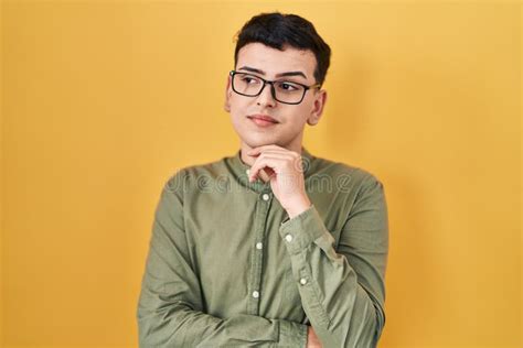 Non Binary Person Standing Over Yellow Background With Hand On Chin