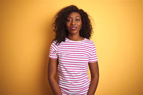 고립 된 노란색 배경 위에 줄무늬 티셔츠를 입은 젊은 아프리카 계 미국인 여성 얼굴에 행복하고 시원한 미소 운이 좋은 사람 T