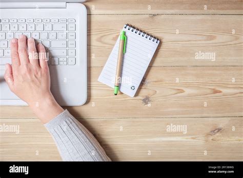 A Top View Of A Womans Hand Typing On A Laptop While A Notepad And Pen Are Visible Beside It