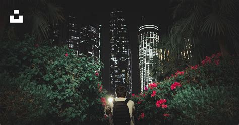조명이 켜진 고층 건물을 마주보고 있는 꽃 사이에 앉아 있는 남자 사진 Unsplash의 무료 에티하드 타워 아부다비 아랍에미리트 이미지