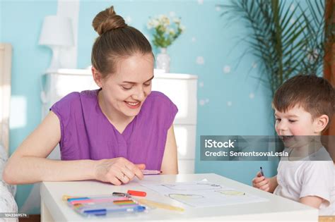 아름 다운 주부 캐주얼 보라색 티셔츠에 그녀의 작은 아들과 자유 시간을 보낸다 다채로운 마커를 사용 하 여 그림 그리기에 대 한 아늑한 국내 인테리어에 대 한 포즈 유년기와