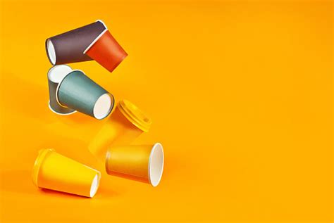 일회용 종이 컵은 주황색 배경에 떨어집니다 다른 크기와 색상의 안경이 닫힙니다 요리 근처에 텍스트를 위한 공간과 여유 공간을