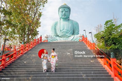 일본식 드레스를 입은 두 명의 아시아계 젊은 여성이 낮의 빛을 배경으로 녹색 큰 불상이 있는 계단을 내려온다 부처 불교에 대한 스톡 사진 및 기타 이미지 Istock
