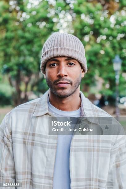 비니 모자를 쓴 젊은 매력적인 아프리카계 미국인 남성의 개별 초상화를 세로로 클로즈업하고 카메라를 진지하게 쳐다본다 슬픈 태도로 야외 공원에 서 있는 히스패닉계 남자의 정면