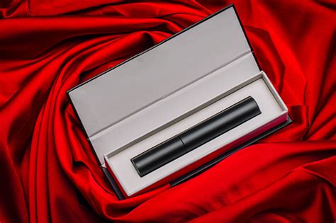 열린 흰색 선물 상자에 담긴 우아한 검은색 펜으로 고급스러운 주름이 있는 풍부한 빨간색 새틴 패브릭에 배치되어 프리미엄 제품 또는 선물 프레젠테이션 테마에 이상적입니다 0