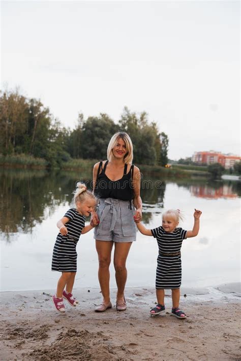 Uma Das Meninas G Meas Pula Perto Do Lago De Parque Perto De Sua M E E Irm Foto De Stock