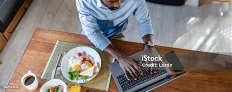한 남자가 아침 식사 접시 커피 주스를 옆에 두고 식탁에서 노트북으로 작업을 하고 있습니다 이 이미지는 위에서 내려다보는